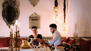 Uma área de refeições com uma mesa posta para dois, candelabros elaborados e um espelho na parede.