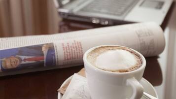 Um laptop sobre uma mesa com uma chávena de café e um jornal.