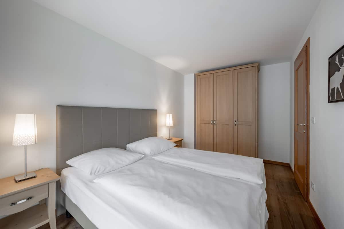 Quarto com cama de casal, mesas de cabeceira com luminárias, guarda-roupa e porta com arte de veado.