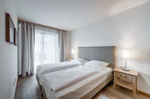 Quarto de hotel com uma cama grande, duas mesas de cabeceira e uma janela com cortinas.