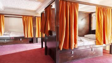 Quarto de hotel com quatro camas de solteiro, cada uma com estrutura de madeira e cortinas laranja.