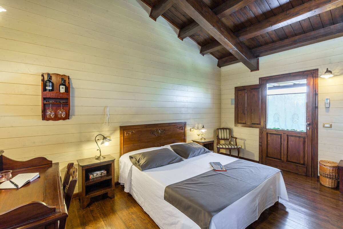 Quarto com cama de madeira, mesas de cabeceira, escrivaninha e uma cadeira.