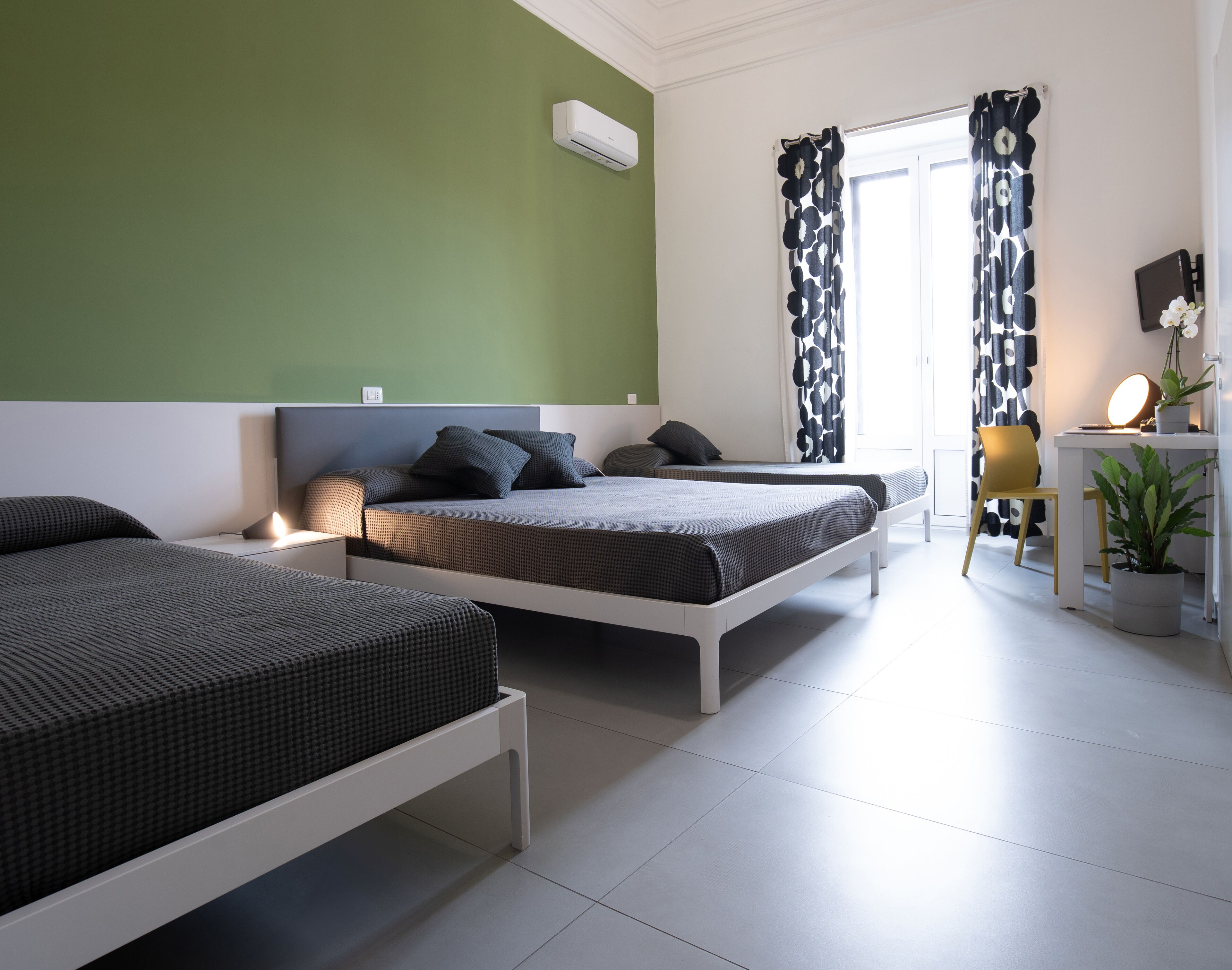 Quarto moderno com duas camas de solteiro, uma escrivaninha com luminária e um vaso com planta.