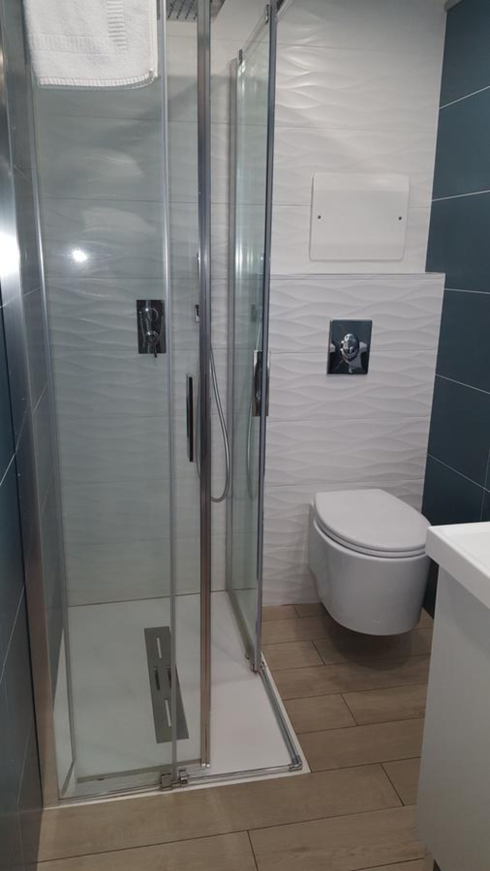 Uma casa de banho moderna com chuveiro envolto em vidro, sanita branca e chão em mosaico.