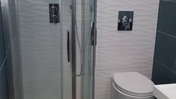 Uma casa de banho moderna com chuveiro envolto em vidro, sanita branca e chão em mosaico.