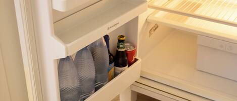 Uma geladeira branca com compartimento para congelador, contendo uma garrafa de cerveja, uma lata de refrigerante e um saco de compras.