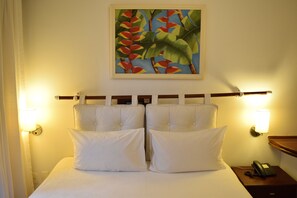 Quarto de hotel com uma cama, duas luminárias de cabeceira, mesa de cabeceira com telefone e um quadro na parede.