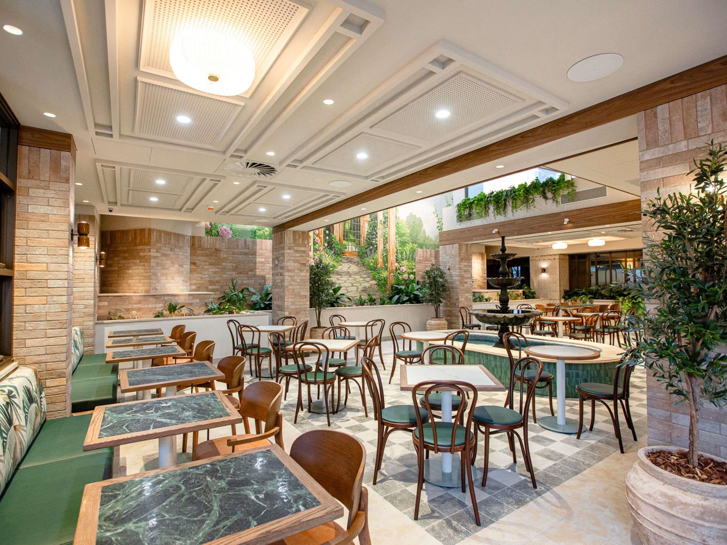 Restaurante com mesas internas, uma fonte e vista para o exterior.