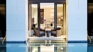 Um saguão de hotel com piscina, duas poltronas, uma mesa e um vaso de flores.