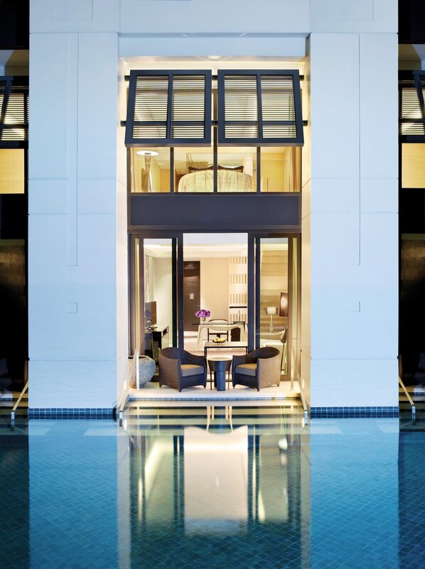 Um hotel moderno com piscina, destacando uma entrada de dois andares, área de jantar com mesa e cadeiras, e uma varanda visível.