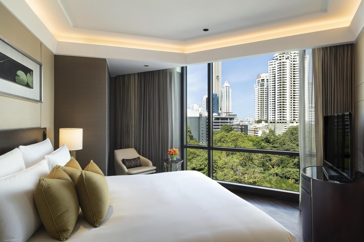 Quarto de hotel com uma cama grande, uma cadeira, uma TV e janela com vista para a cidade.