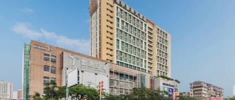 Um hotel com vários andares, um letreiro chamativo, estacionamento e céu azul.