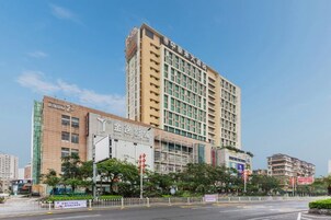 Um hotel com vários andares, um letreiro chamativo, estacionamento e céu azul.