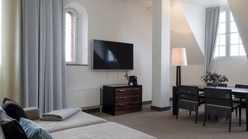 Quarto de hotel moderno com sofá, televisão de tela plana, mesa de jantar com cadeiras e luminária.