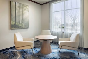 Um quarto com uma mesa redonda, duas cadeiras, uma janela ampla e uma pintura com tema de floresta na parede.