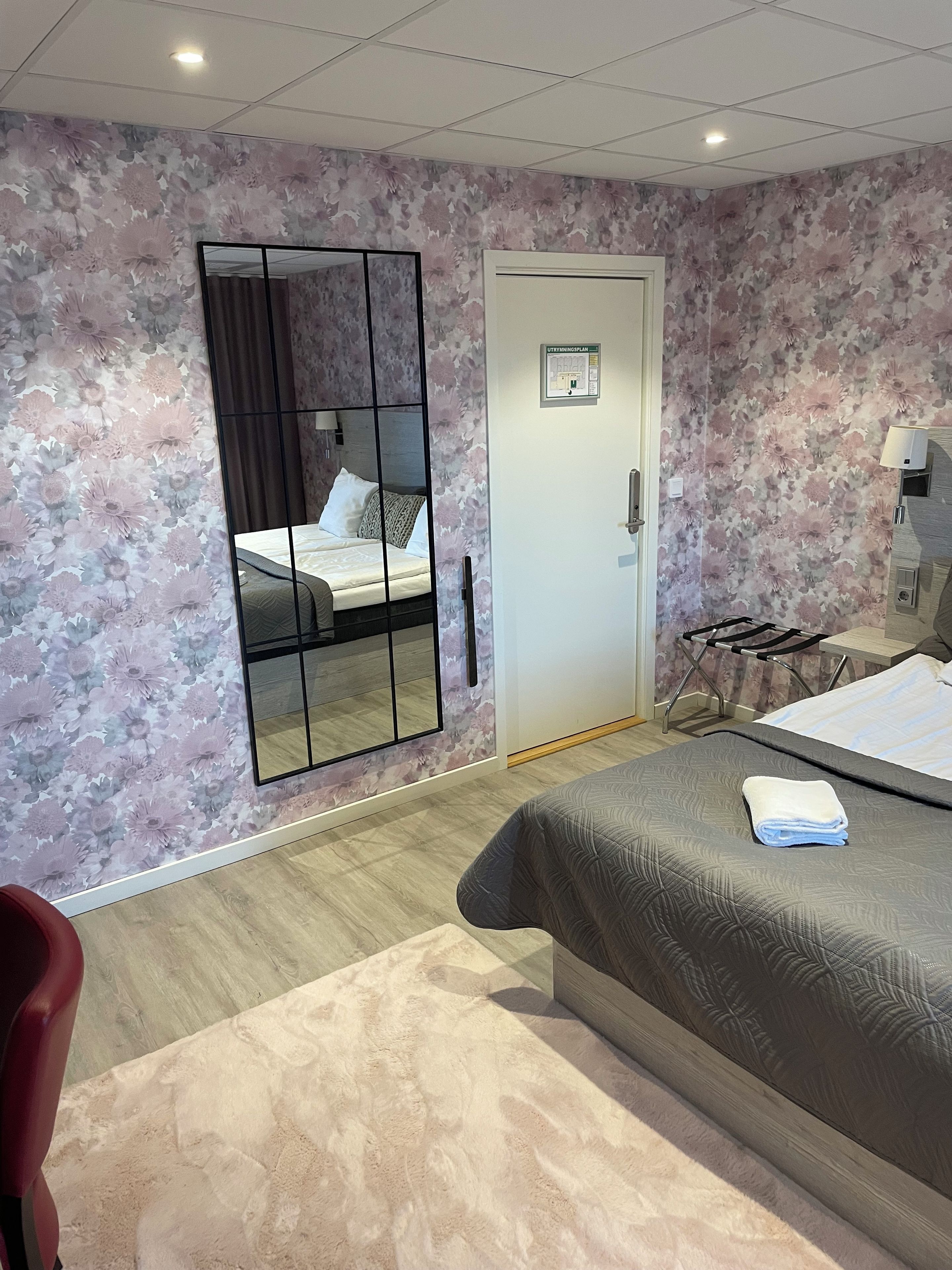 Quarto de hotel com cama, espelho, escrivaninha e cadeira.
