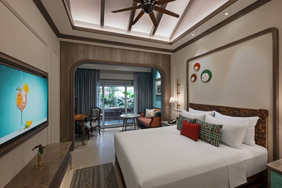 Quarto de hotel com uma cama grande, uma escrivaninha, uma cadeira e uma TV. Possui uma varanda com vista para o verde.