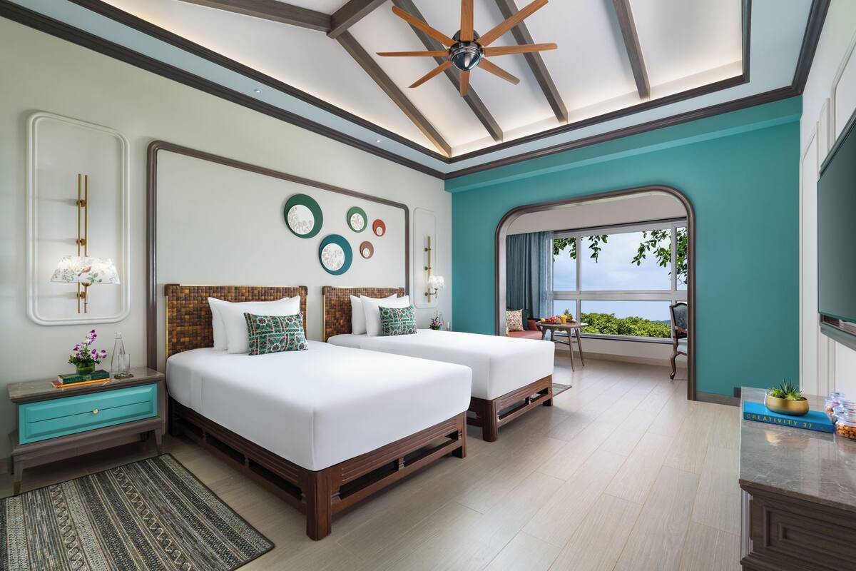 Quarto moderno com duas camas, ventilador de teto e vista para o exterior.