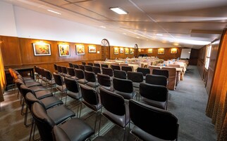 Uma sala de conferências com fileiras de cadeiras e mesas, painéis de madeira e quadros nas paredes.