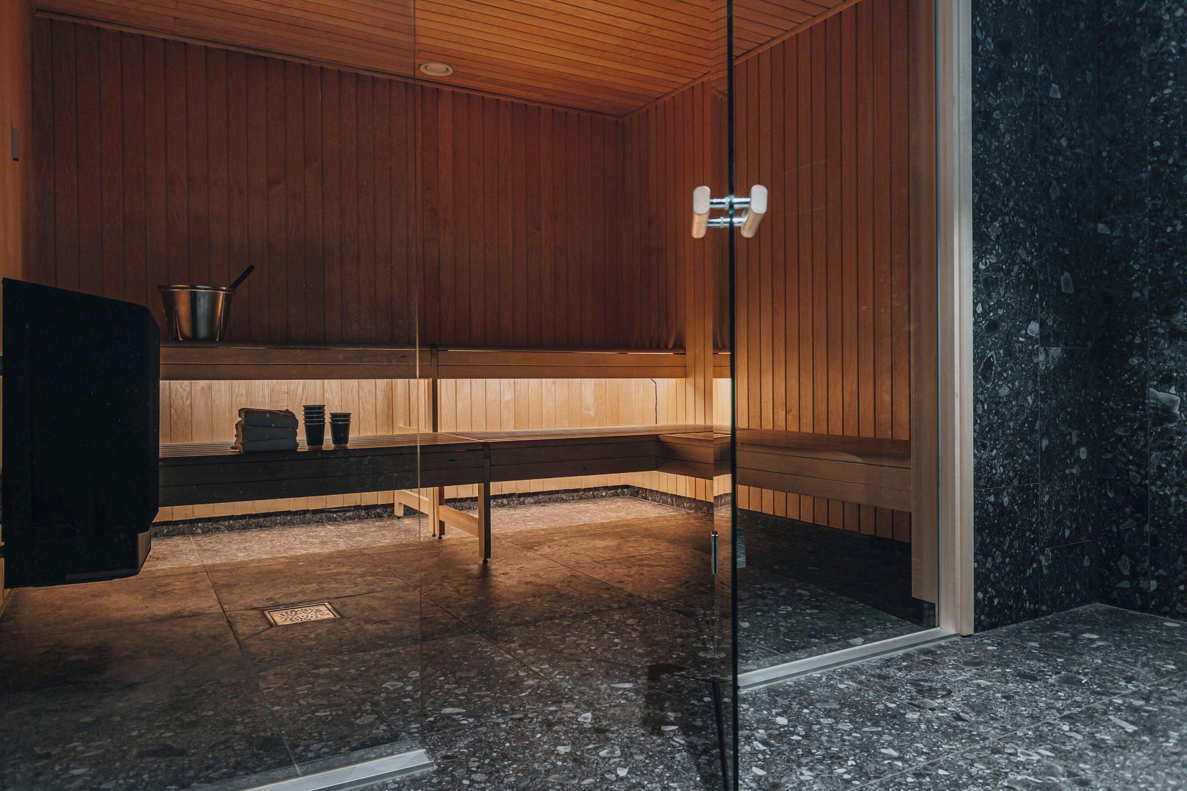 Uma sauna com bancos de madeira, um balde de metal e uma porta de vidro.