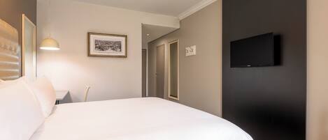 Quarto de hotel com uma cama grande, uma televisão de tela plana fixada na parede, um quadro pendurado na parede e uma porta que dá para outro cômodo.