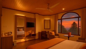 Quarto de hotel com uma cama grande, uma escrivaninha, uma cadeira, uma televisão e janela com vista para o pôr do sol.