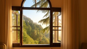 Quarto com uma grande janela em arco que oferece vista para um vale verdejante.