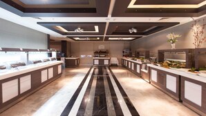 Um lobby de hotel moderno com piso listrado em preto e branco, várias estações de buffet e luminárias contemporâneas.