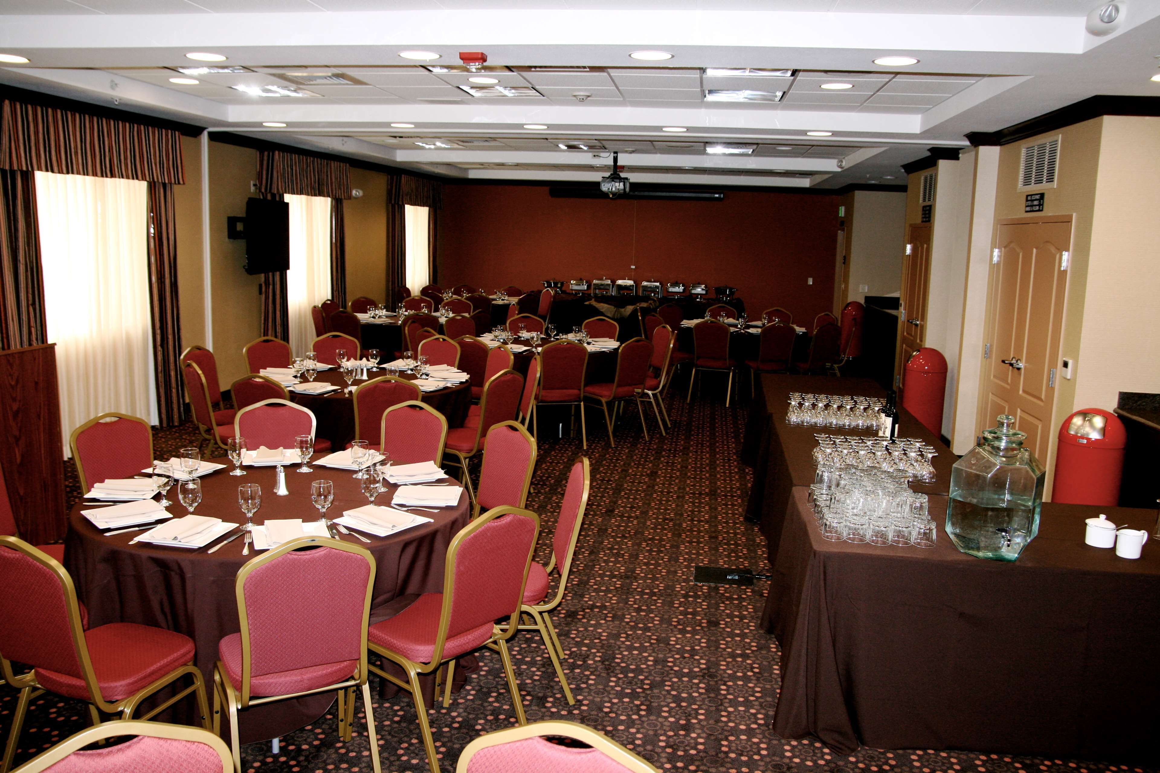 Sala de conferências com várias mesas redondas, cadeiras vermelhas e uma tela de projeção.