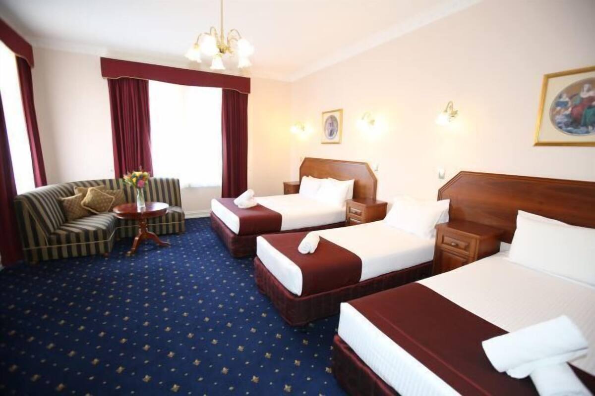 Quarto de hotel com duas camas, um sofá, uma mesa pequena e um candelabro.