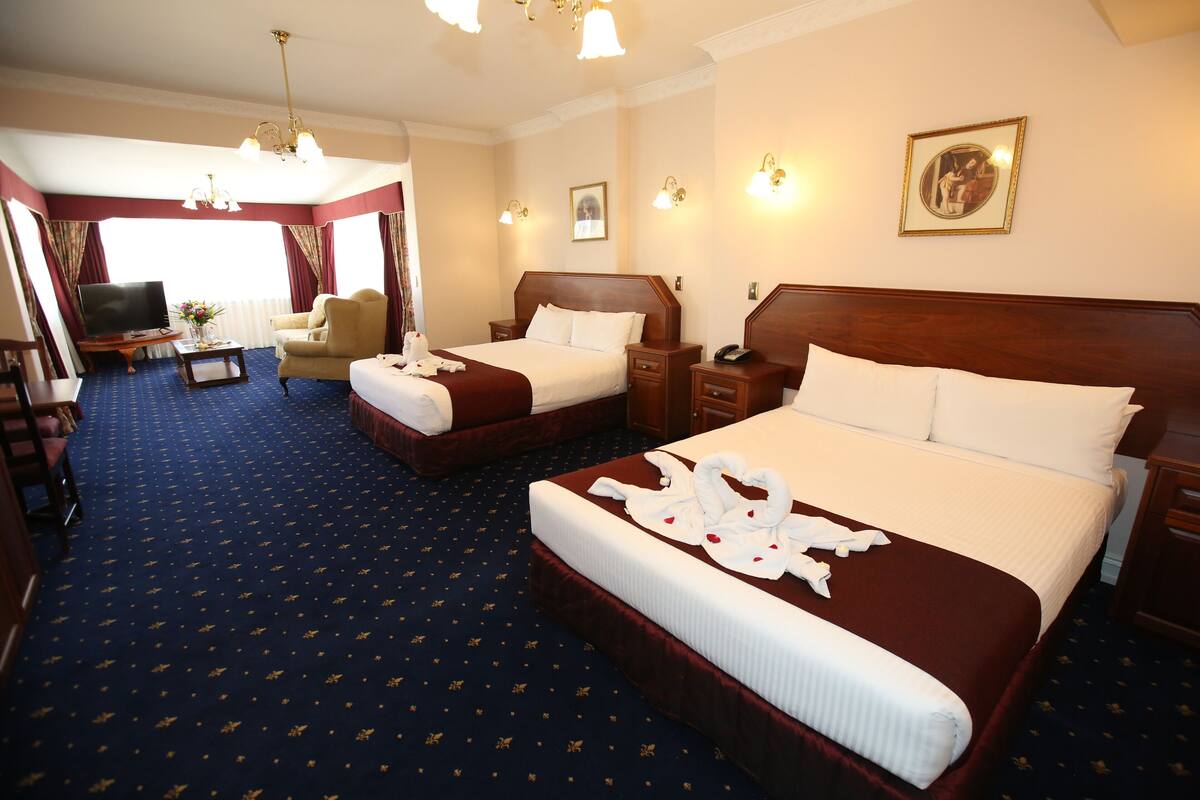 Quarto de hotel com uma cama grande, duas camas menores, uma televisão, uma escrivaninha e uma cadeira.