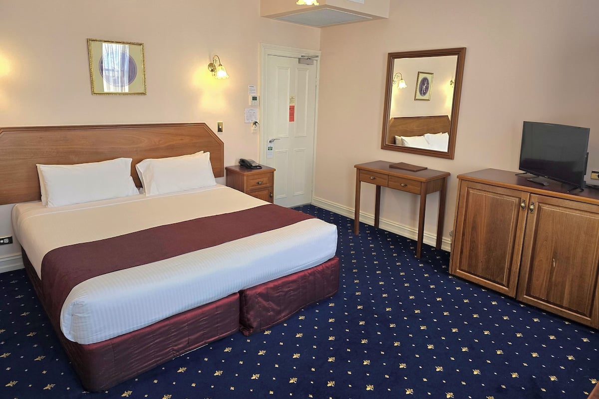 Quarto de hotel com uma cama grande, mesas de cabeceira, uma escrivaninha, televisão e um espelho.