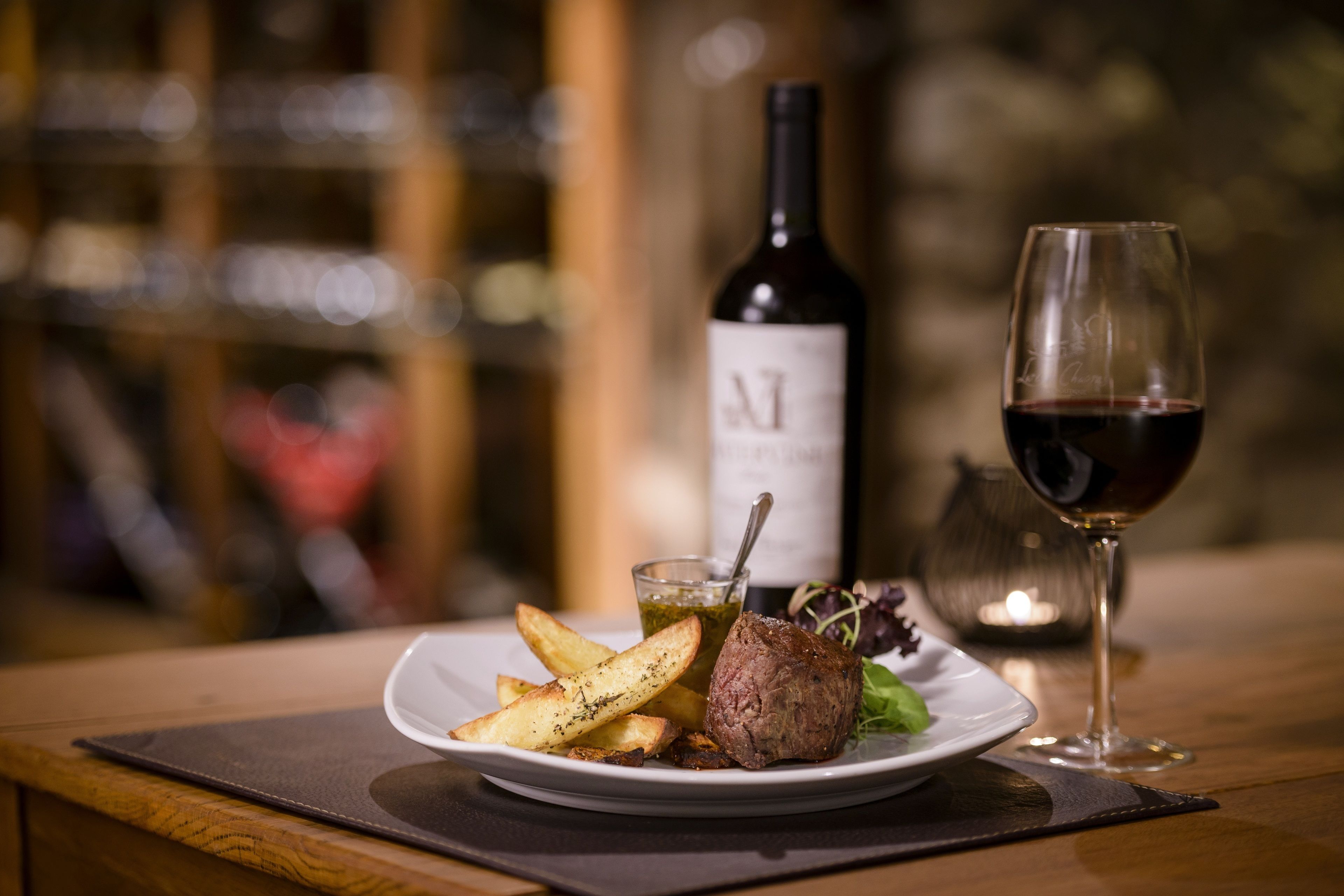 Um prato de comida com uma garrafa de vinho e um copo de vinho tinto sobre uma mesa de madeira.