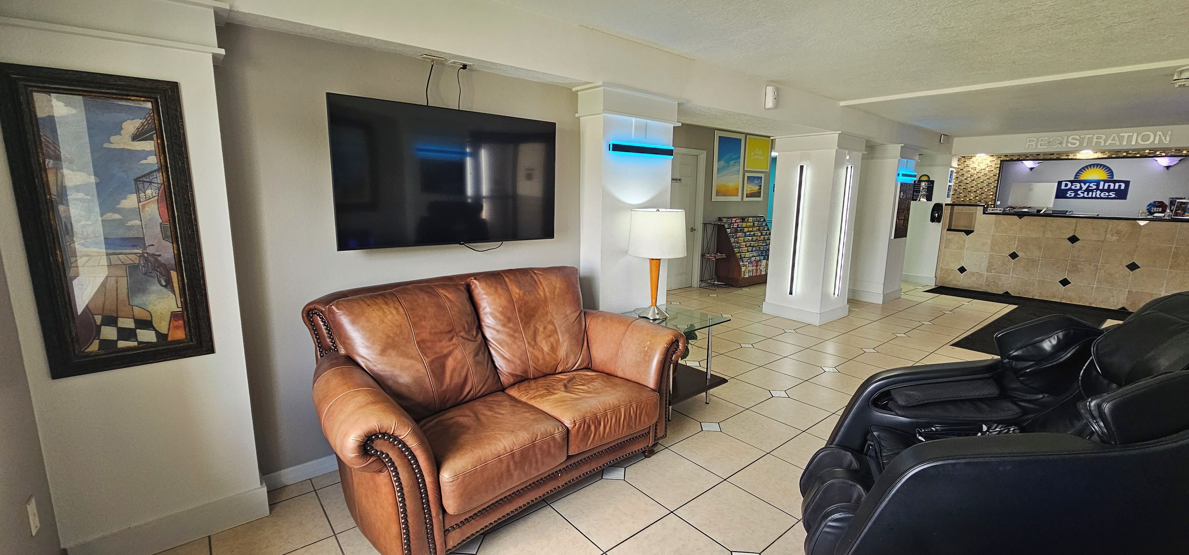 Um saguão de hotel com sofá de couro, televisão de tela plana, balcão de recepção e poltrona de massagem.