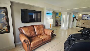 Um saguão de hotel com sofá de couro, televisão de tela plana, balcão de recepção e poltrona de massagem.