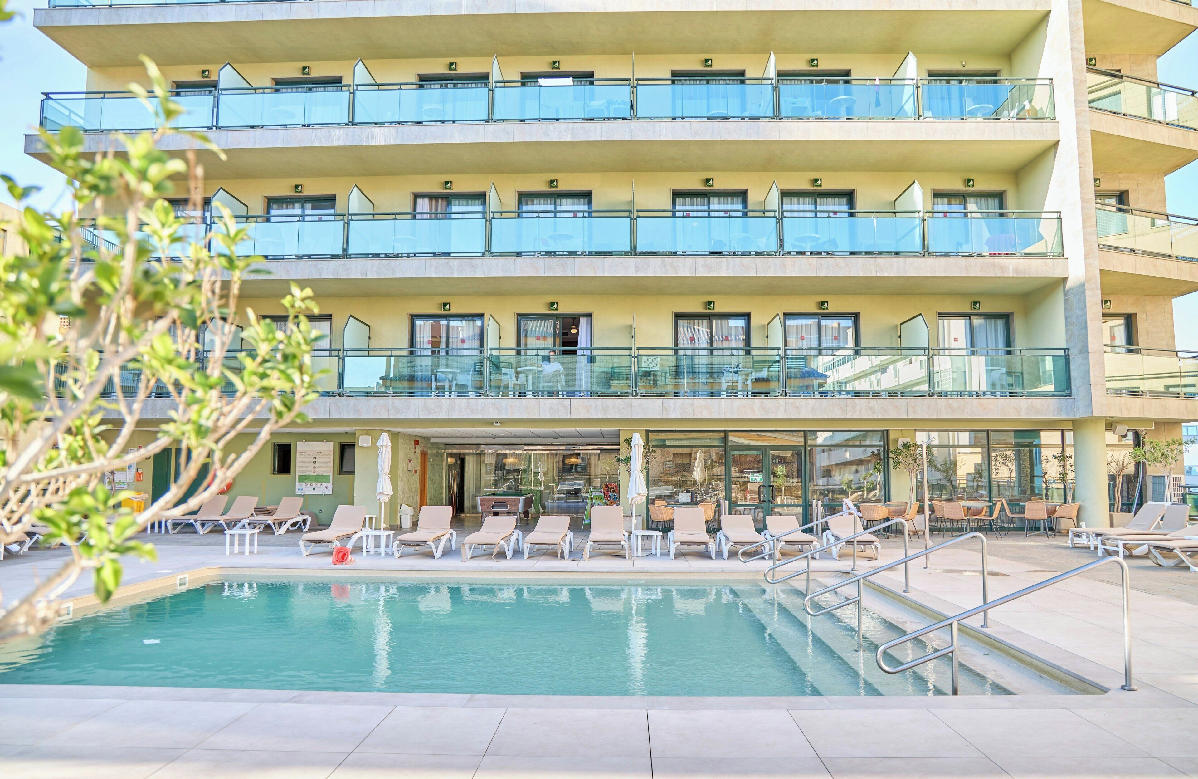 Um hotel com piscina, várias varandas e área de estar externa.