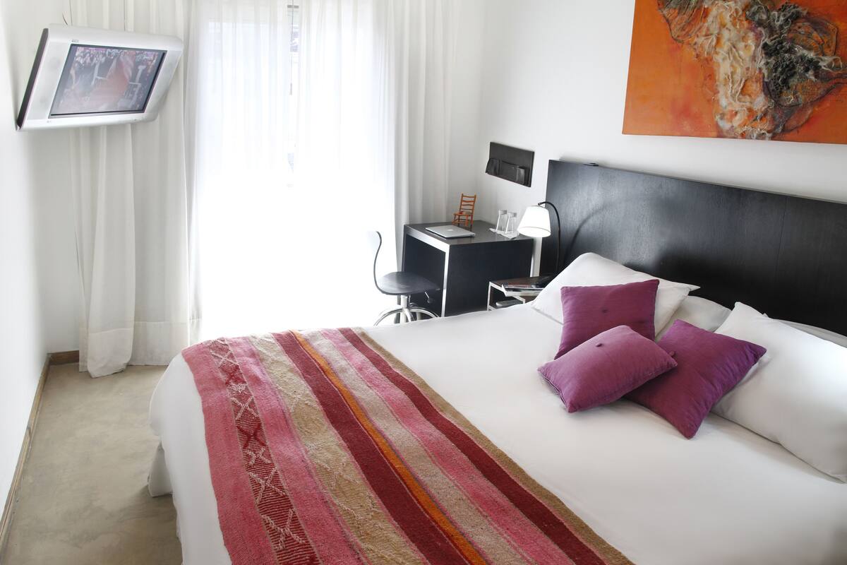 Quarto de hotel com uma cama grande, uma escrivaninha com computador, uma cadeira e um quadro na parede.
