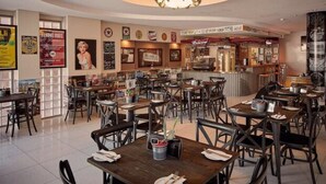 Um restaurante com várias mesas e cadeiras, um espaço de bar e diversos cartazes nas paredes.