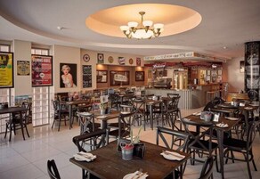 Um restaurante com várias mesas e cadeiras, um espaço de bar e diversos cartazes nas paredes.