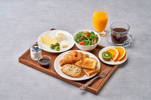 Bandeja de café da manhã com croissants, torradas, uma salada, um copo de suco de laranja, uma xícara de café e um copo de leite.