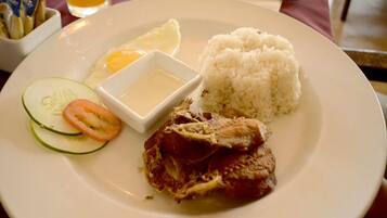 Um prato com arroz, um pedaço de carne, uma fatia de limão, uma pequena tigela de molho e uma fatia de pepino.