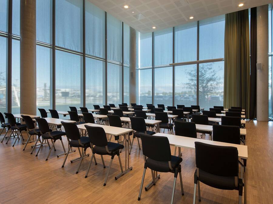 Sala de conferências com grandes janelas, várias mesas e cadeiras pretas.
