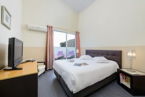 Quarto de hotel com cama, escrivaninha com computador, televisão, janela com cortinas e vista para o exterior.
