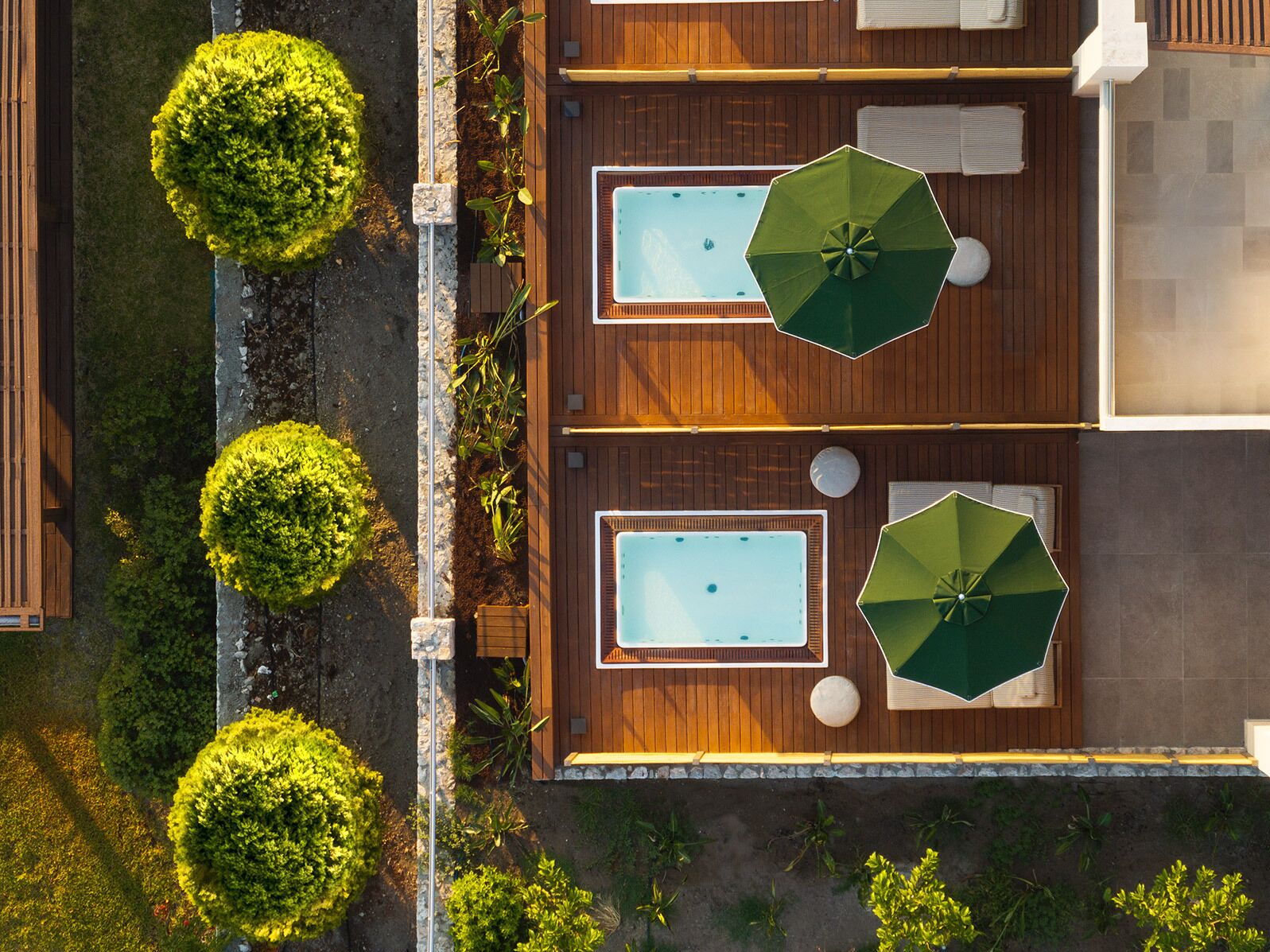 Vista aérea de um terraço com duas piscinas, rodeado por um deck de madeira e guarda-sóis verdes.