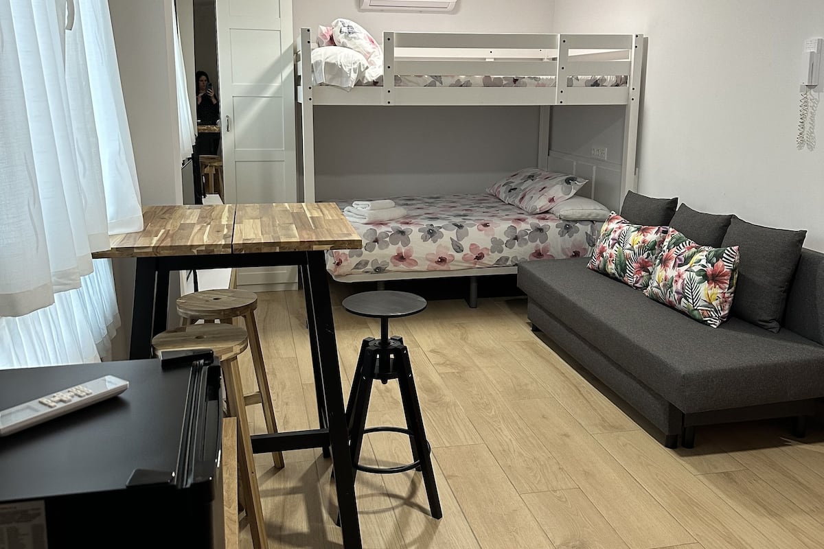 Um espaço compacto com beliche, sofá, mesa pequena e um banquinho.