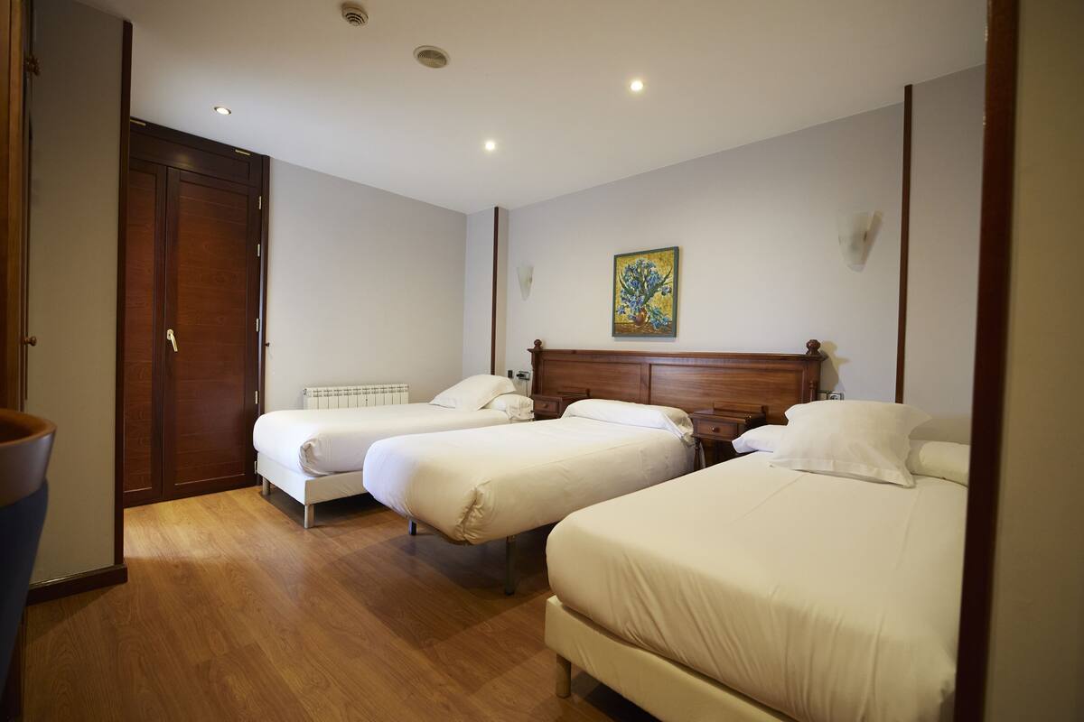 Quarto de hotel com duas camas individuais, soalho de madeira, radiador e um quadro na parede.