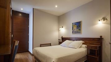 Quarto com cama de madeira, mesas de cabeceira, luminária na parede e uma pintura.