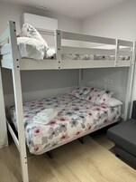 Uma cama beliche com colcha florida e um sofá cinza em um quarto com piso de madeira clara.