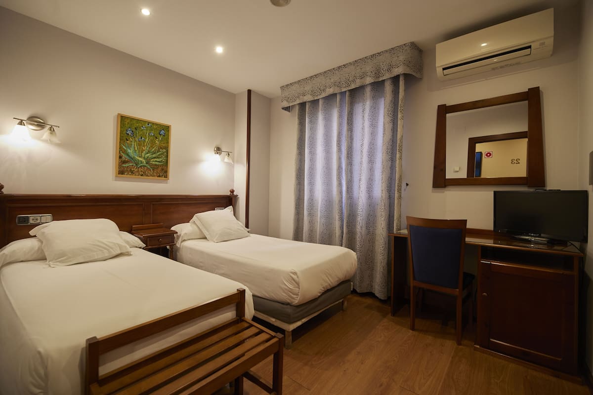 Quarto de hotel com duas camas de solteiro, uma escrivaninha com cadeira, televisão e ar condicionado.