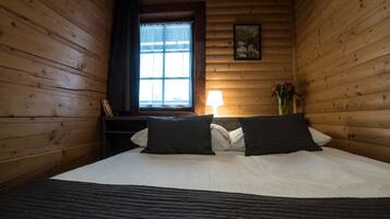 Quarto de cabana de madeira com uma cama, uma janela, um abajur e um quadro na parede.